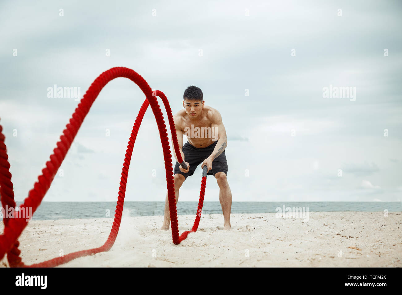 Young healthy man athlete doing exercise with the rope at the beach ...