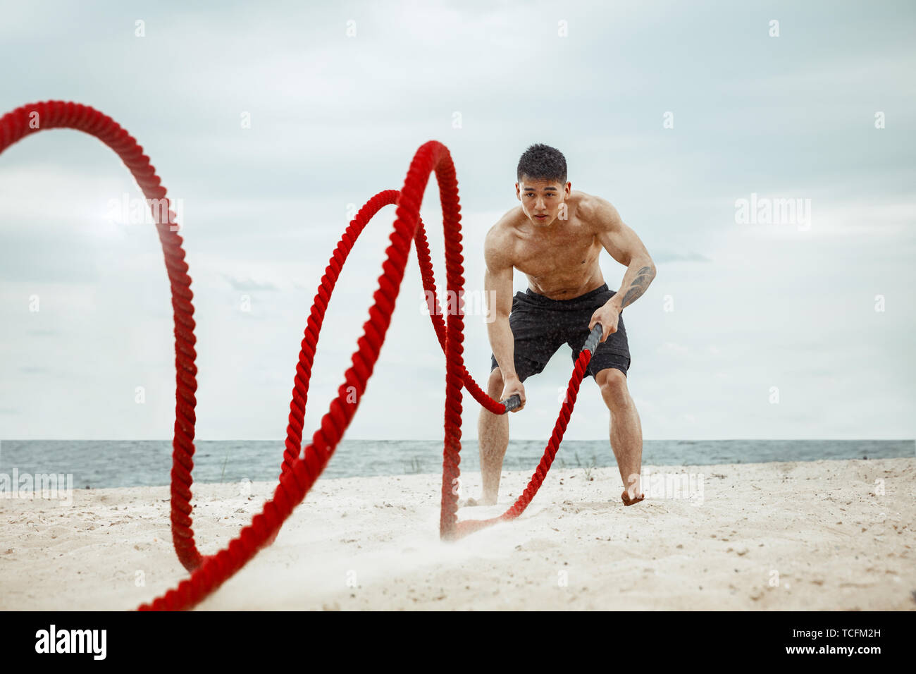 Young healthy man athlete doing exercise with the rope at the beach ...