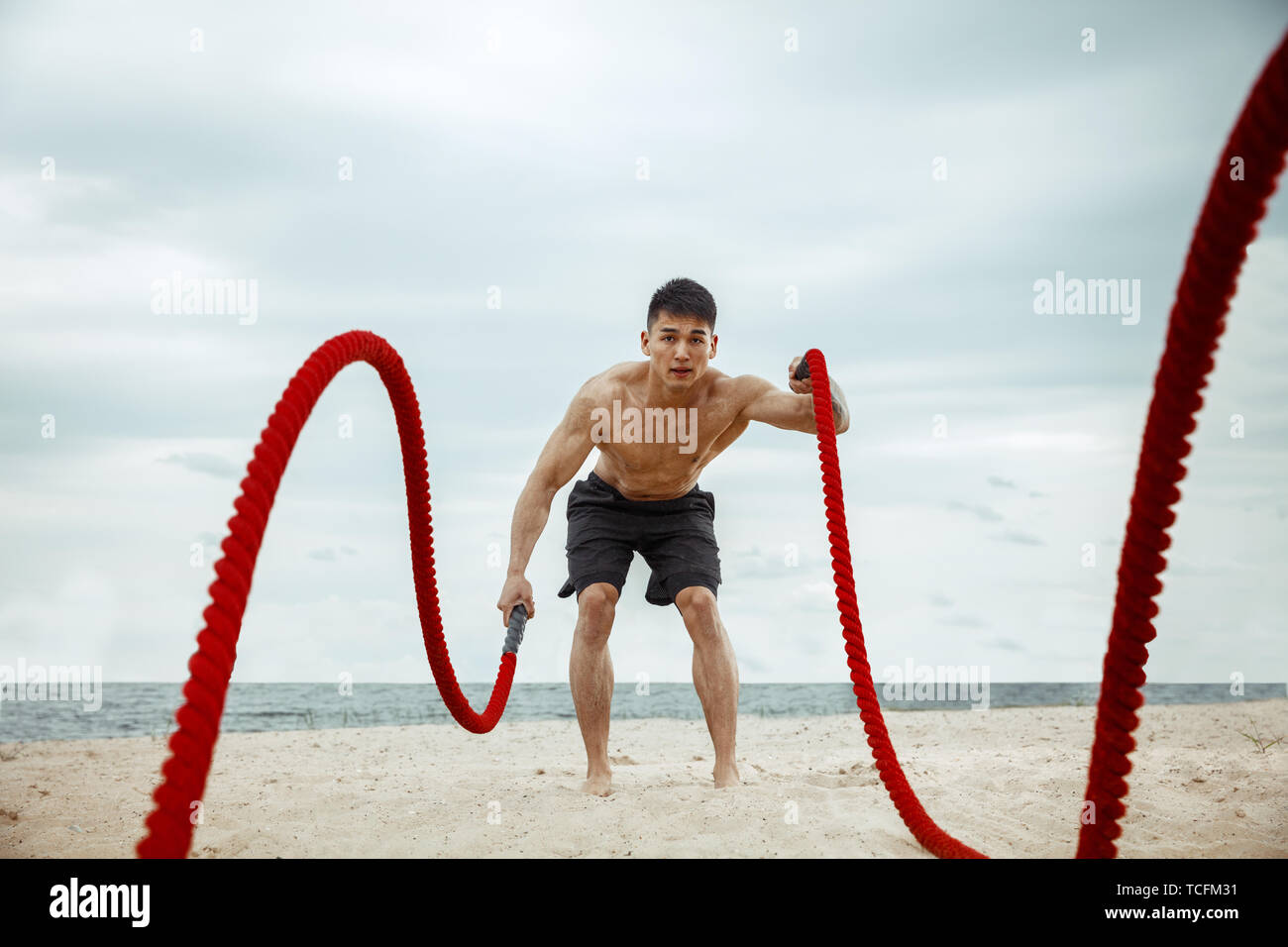 Young healthy man athlete doing exercise with the rope at the beach ...