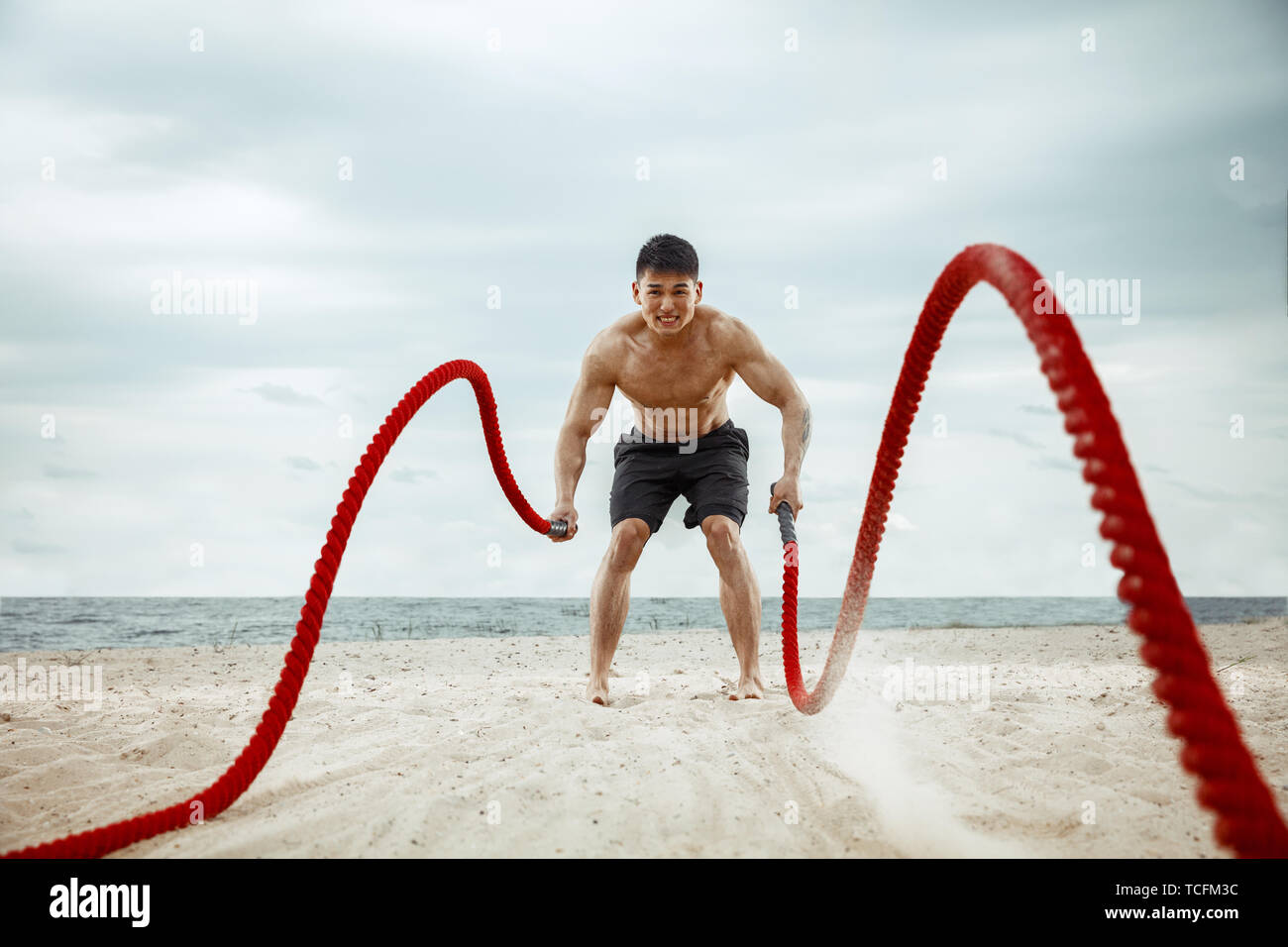 Young healthy man athlete doing exercise with the rope at the beach ...
