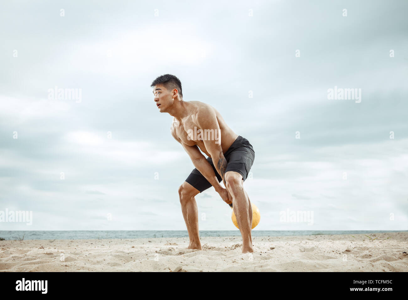 Young healthy man athlete doing exercise with the weight at the beach ...