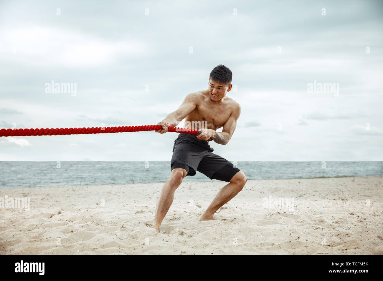 Young healthy man athlete doing exercise with the rope at the beach ...