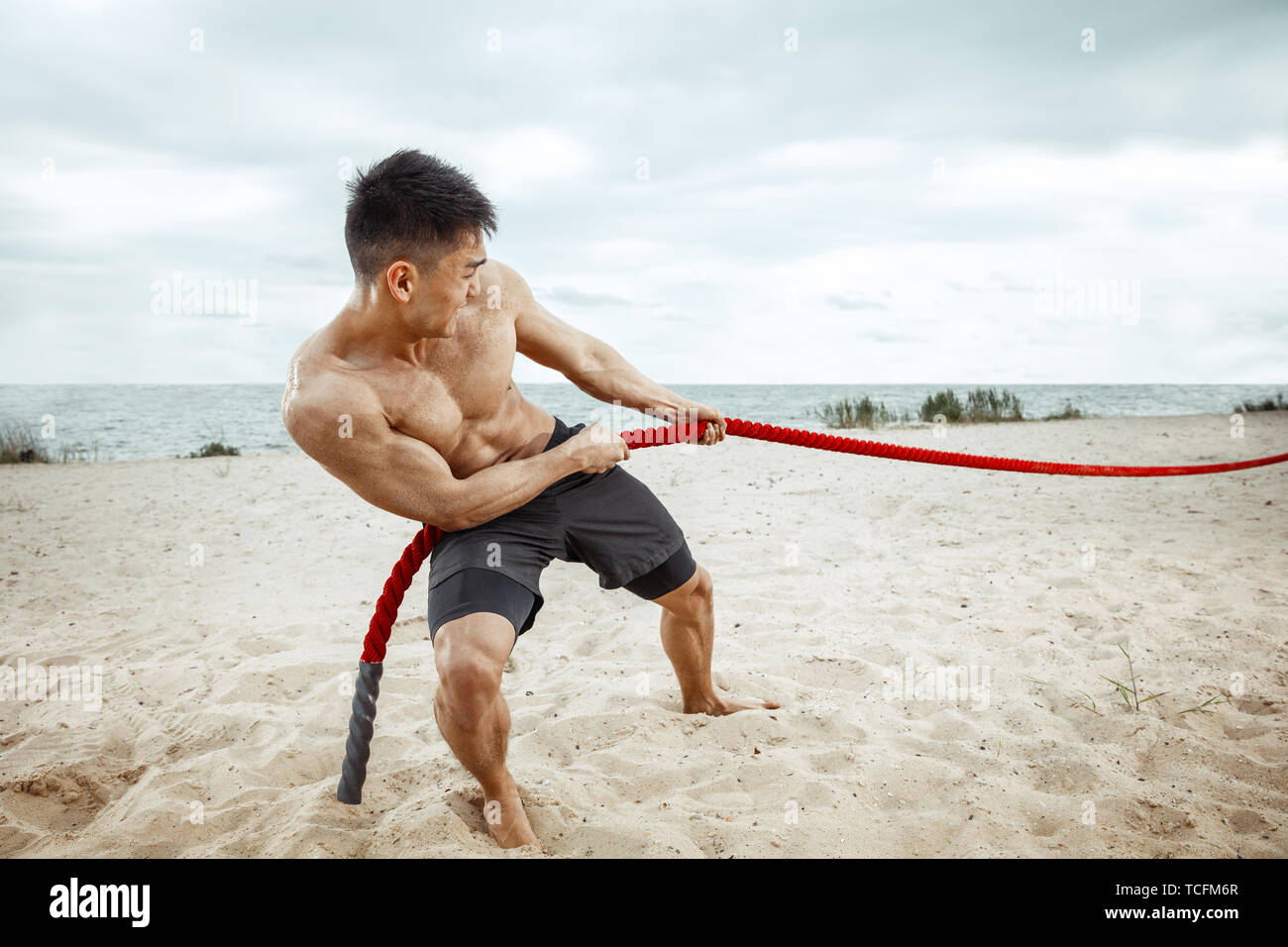 Young healthy man athlete doing exercise with the rope at the beach ...