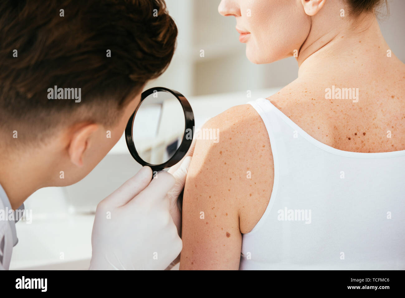 cropped view of dermatologist holding magnifying glass while examining ...