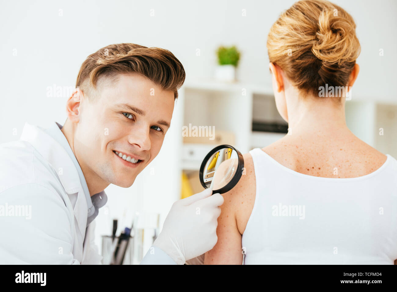 cheerful dermatologist holding magnifying glass while examining woman ...