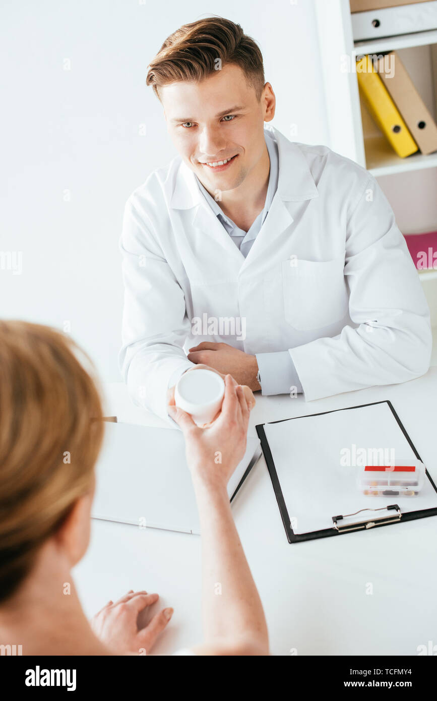 overhead view of cheerful doctor giving container with cosmetic cream ...