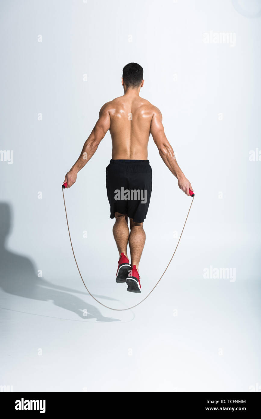 back view of athletic man in black shorts jumping with skipping rope on ...