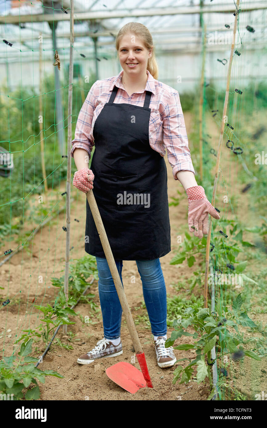 Young female farmer working in greenhouse, hoeing soil on plantation of ...