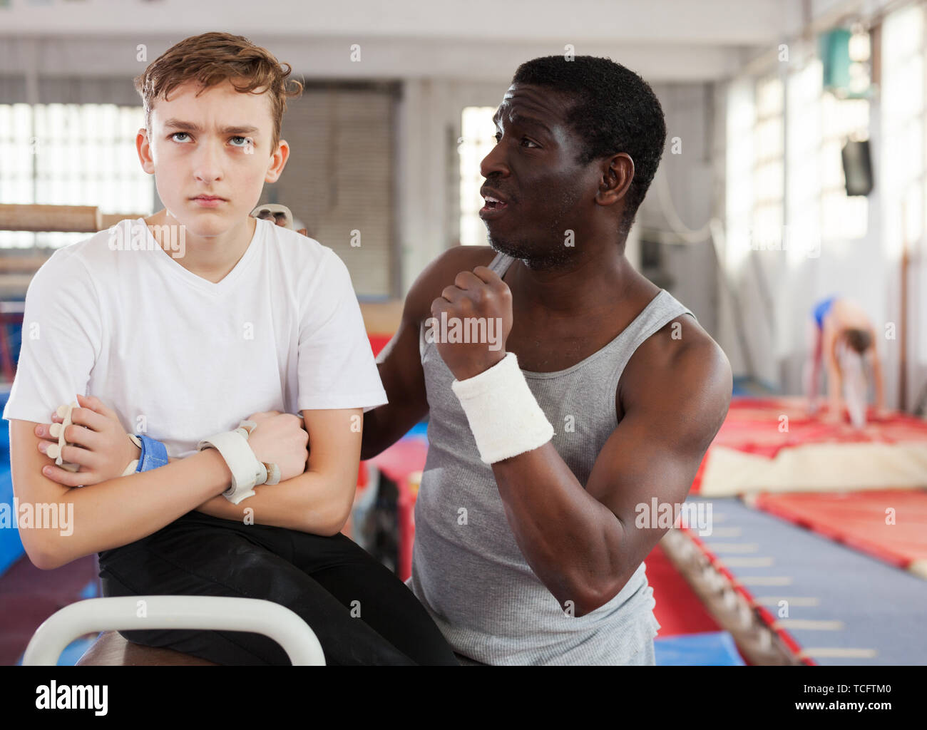 young African coach soothing sad teenage athlete sitting on pommel ...