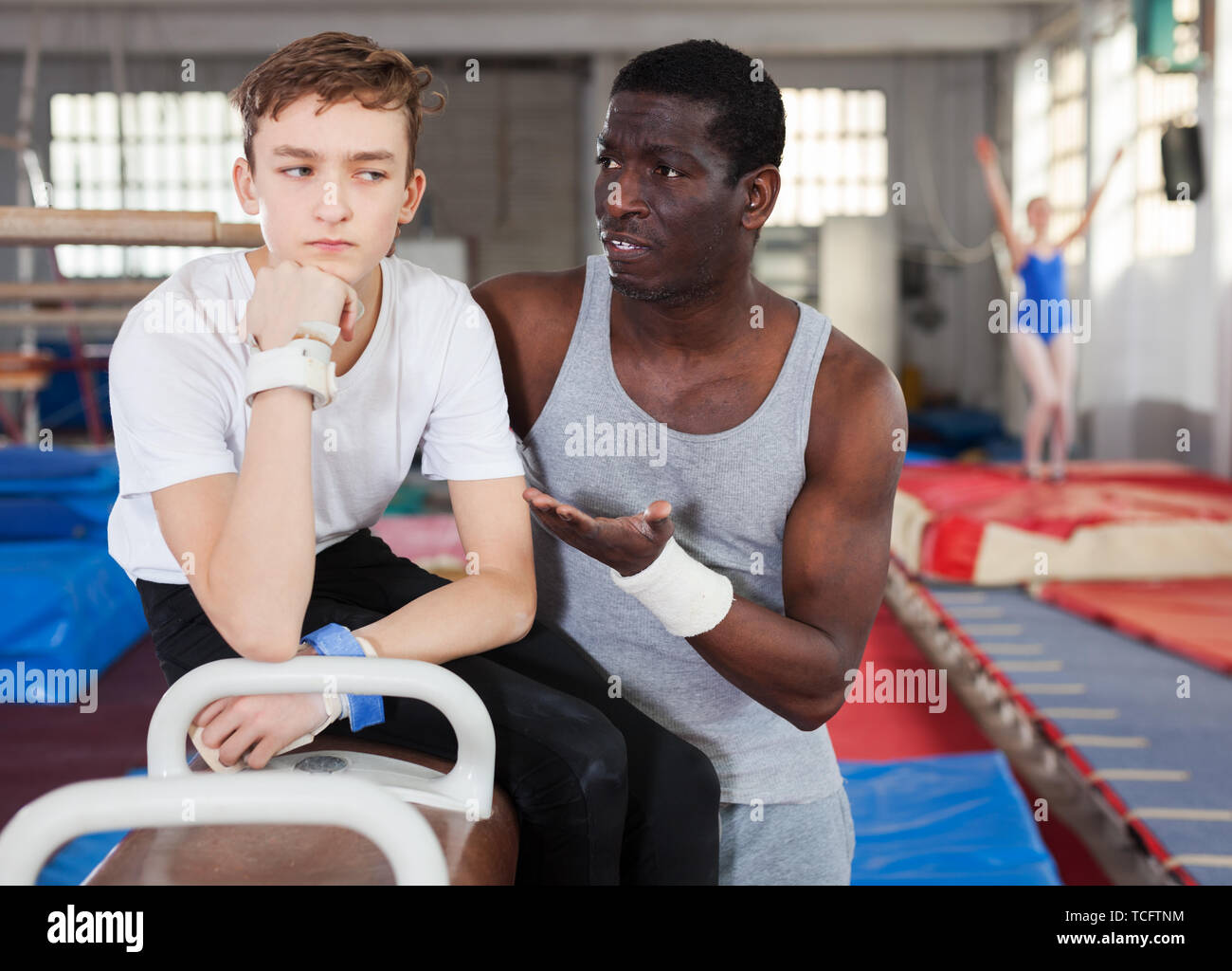Male coach comforting sad teenage boy on gymnastic equipment at sport ...