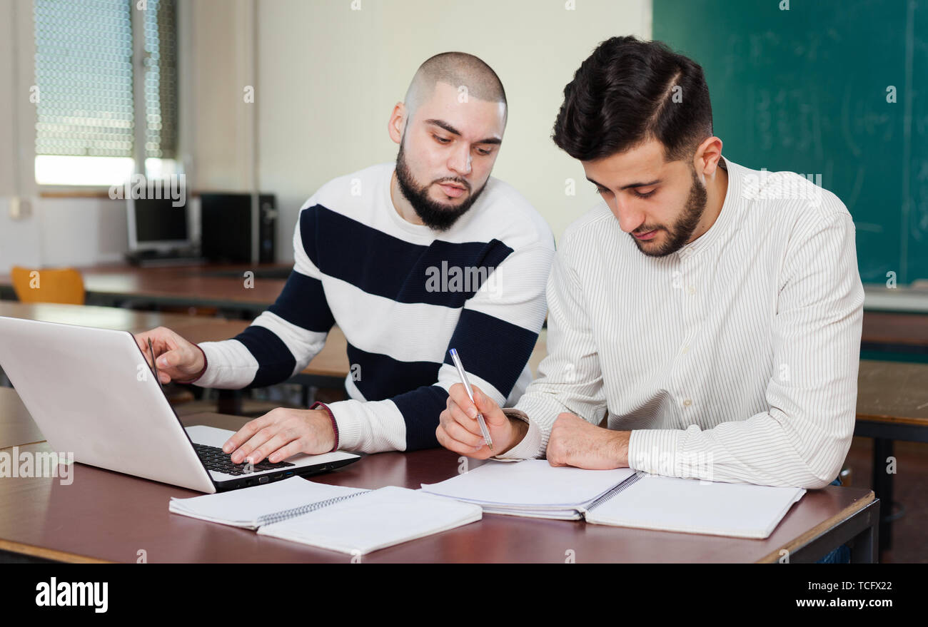 Portrait of two young guys working on their student project at desk in ...