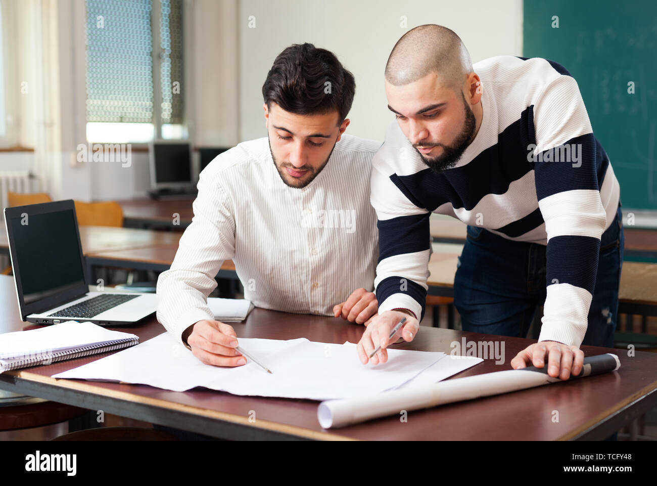 Portrait of two young guys working on their student project at desk in ...