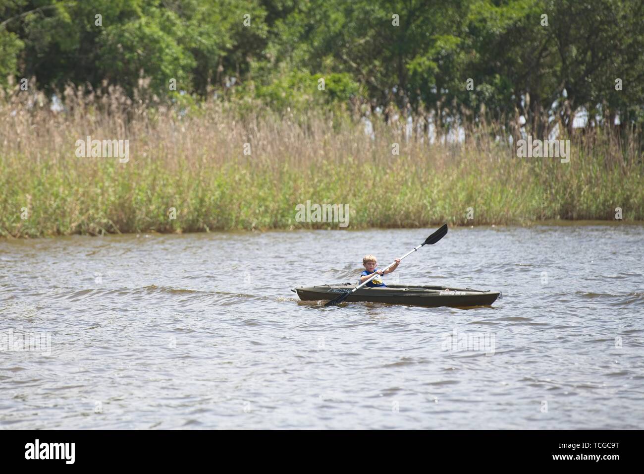 A young boy paddles a kayak along the waterfront of the bay Stock Photo ...