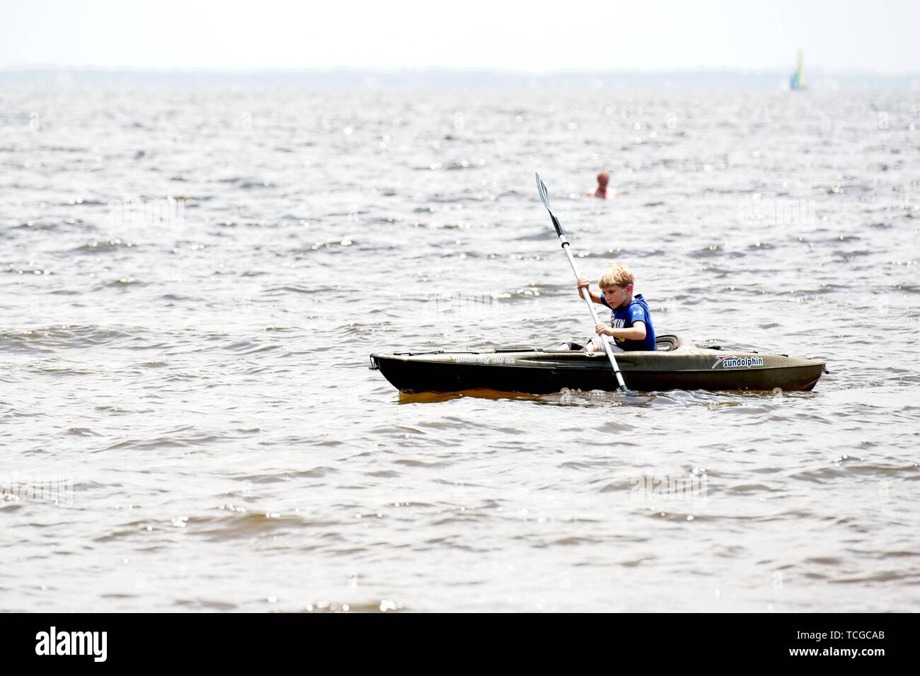 A young boy paddles a kayak along the waterfront of the bay Stock Photo ...