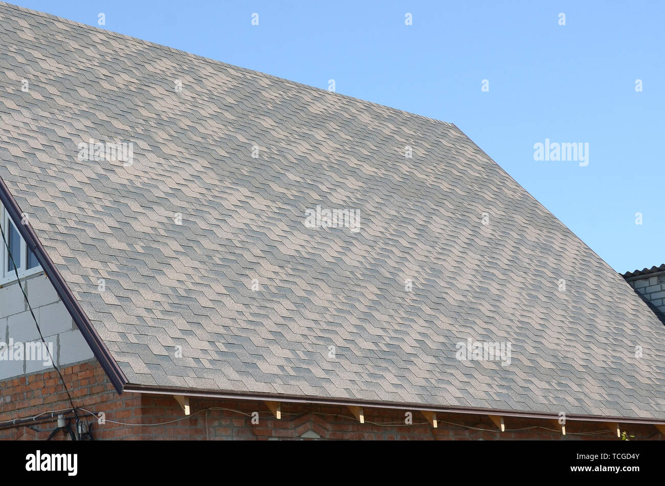 Flexible shingles of bitumen roofing surface on the brick house. Mosaic ...