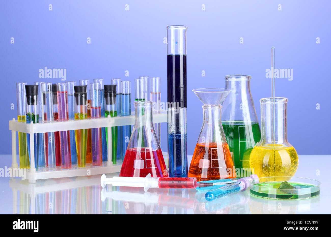 Different laboratory glassware with color liquid on violet background ...