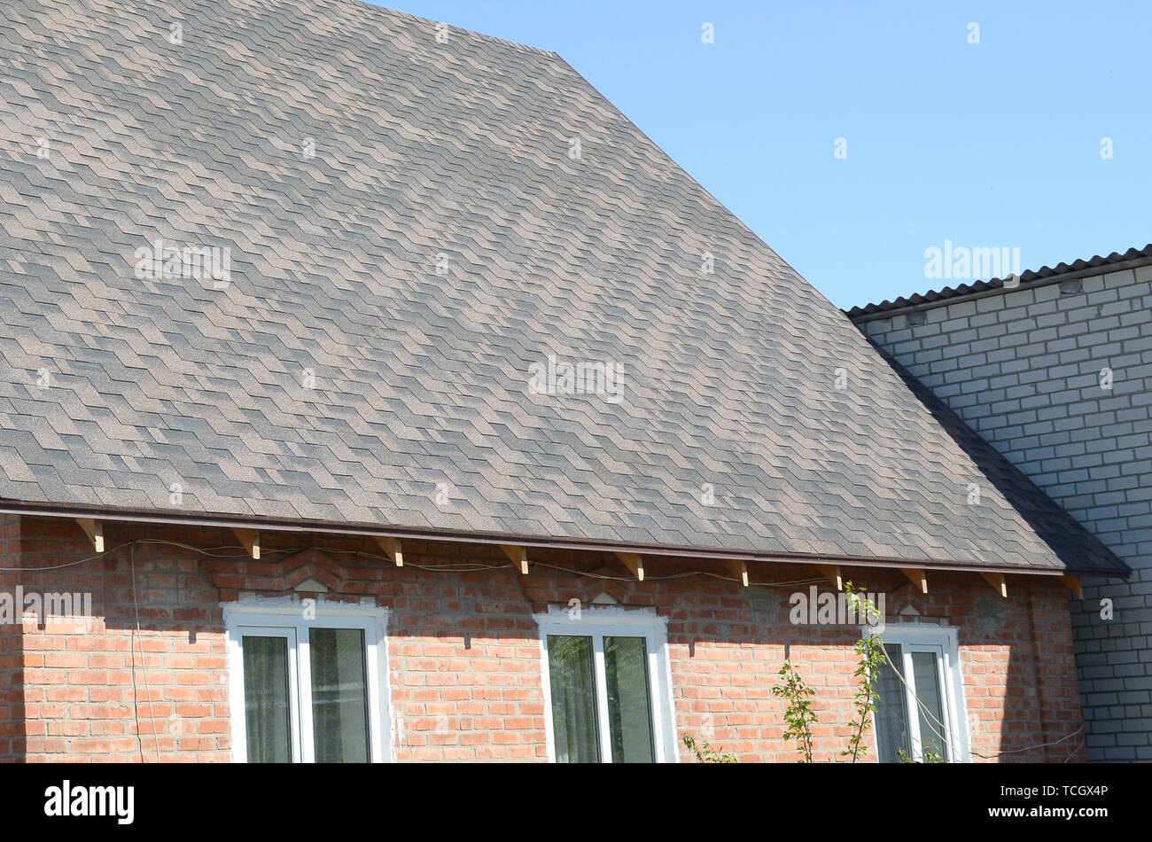 Flexible shingles of bitumen roofing surface on the brick house. Mosaic ...