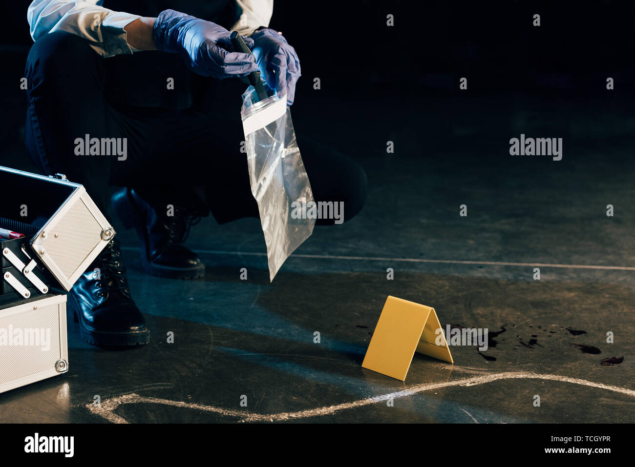 cropped view of investigator in uniform with evidence at crime scene ...