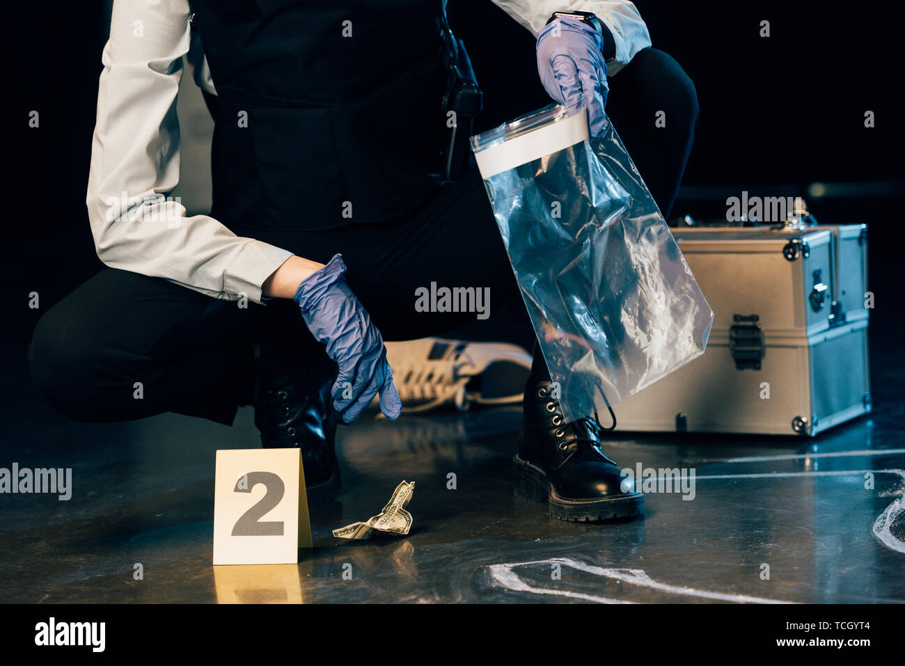 partial view of investigator in uniform collecting evidences at crime ...