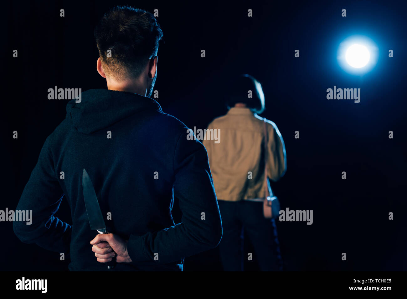 back view view of murderer hiding knife and looking at victim on black ...