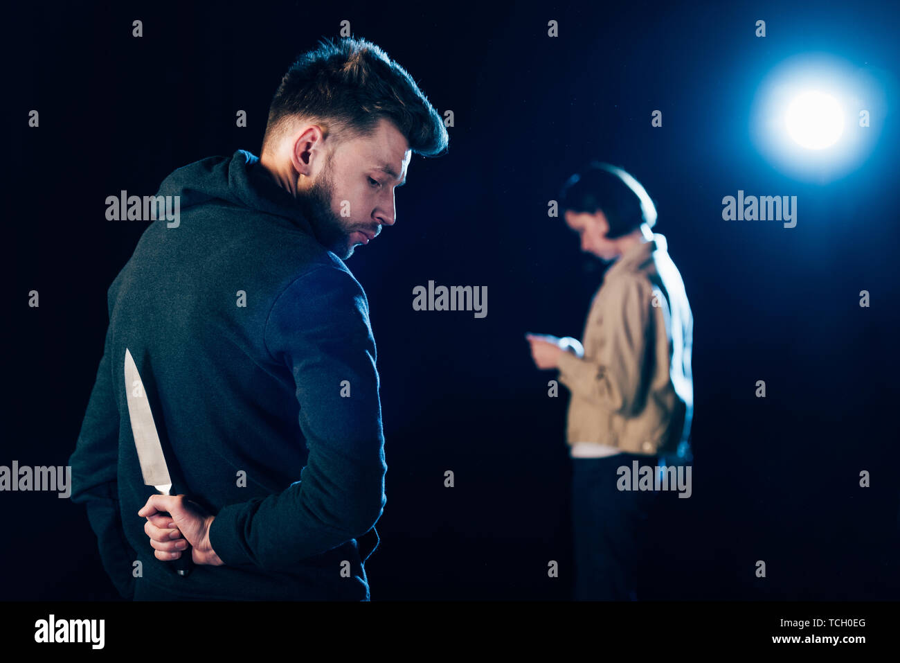pensive murderer hiding knife behind back on black Stock Photo - Alamy