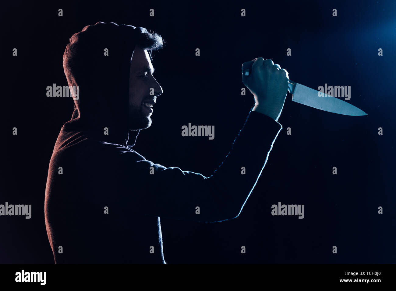 side view of smiling criminal in casual clothes holding knife on black ...