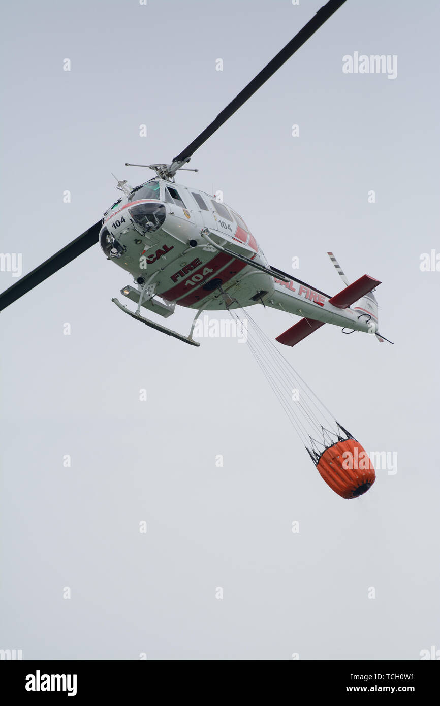 A Cal Fire helicopter flying around with water bucket in lake berryessa ...