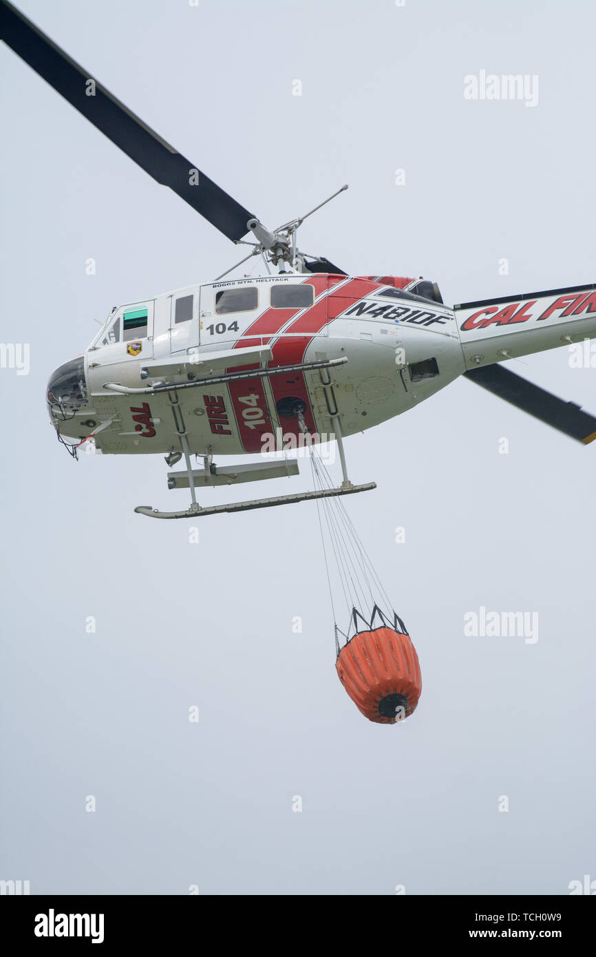 A Cal Fire helicopter flying around with water bucket in lake berryessa ...