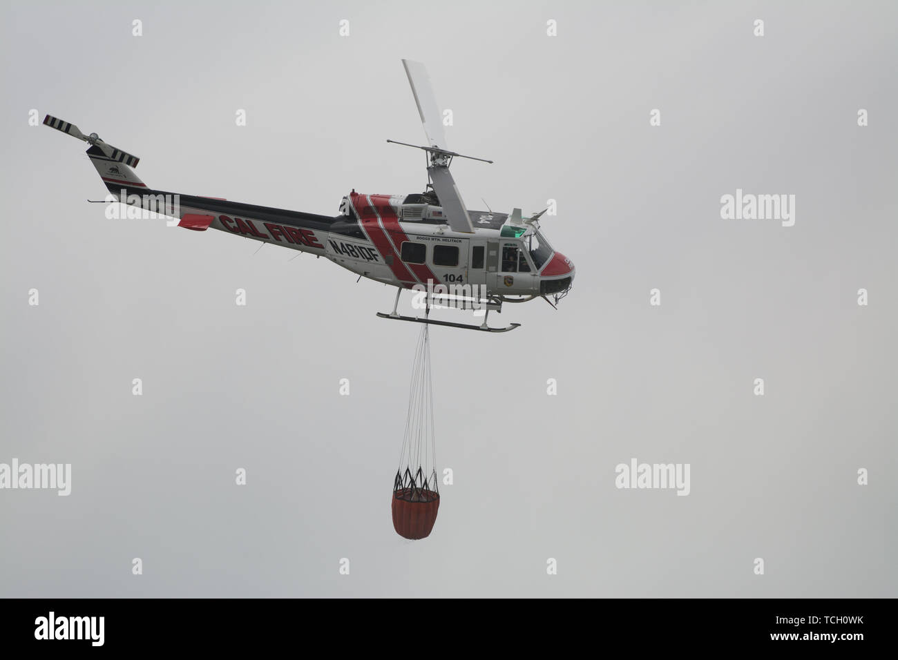 A Cal Fire helicopter flying around with water bucket in lake berryessa ...