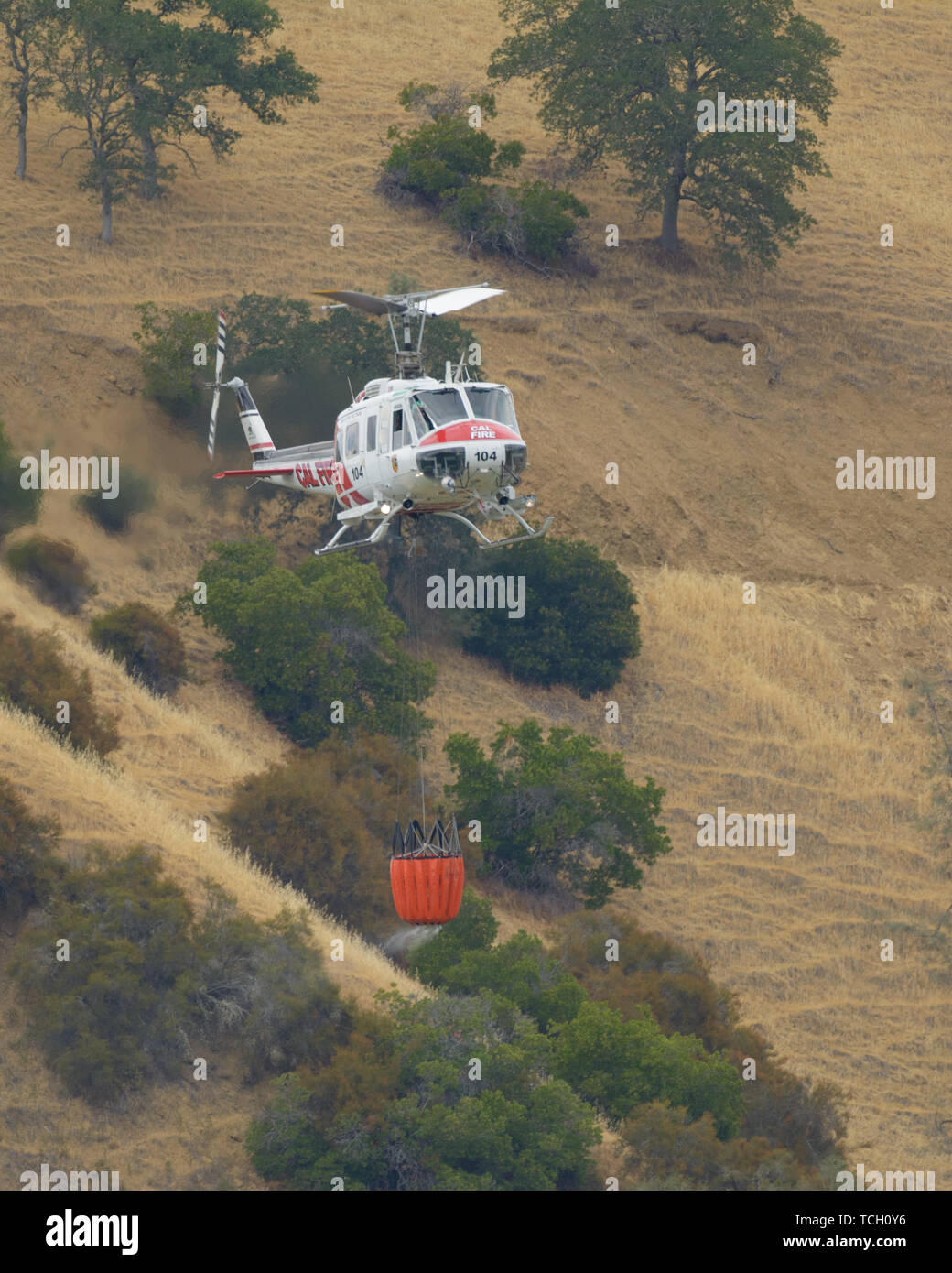 A Cal Fire Helicopter flying through the hills with a water bucket ...