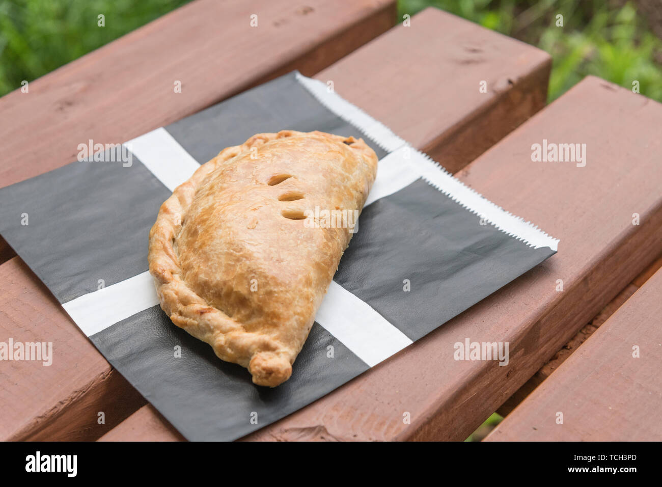 Cornish pasty sitting on paper food bag decorated with St. Piran's flag ...