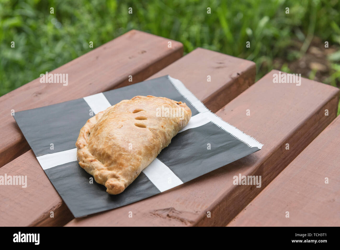 Cornish pasty sitting on paper food bag decorated with St. Piran's flag ...