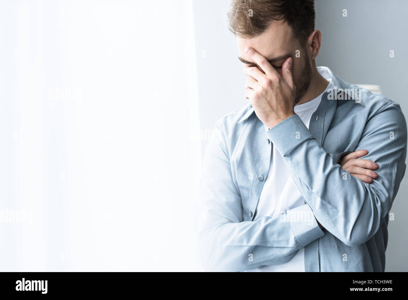 depressed man in blue shirt covering face with hand on at home Stock ...