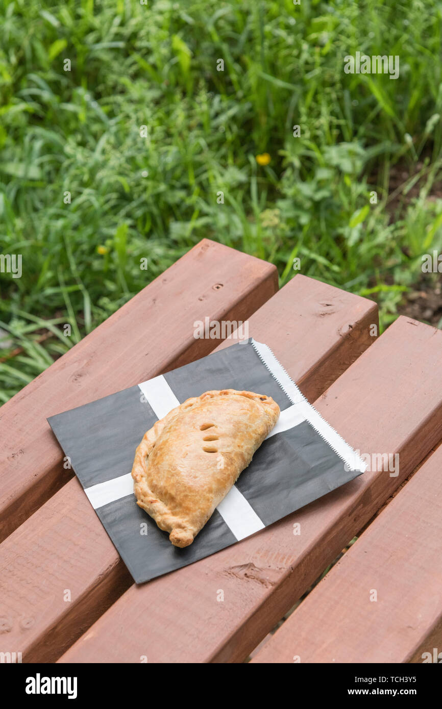 Cornish pasty sitting on paper food bag decorated with St. Piran's flag ...