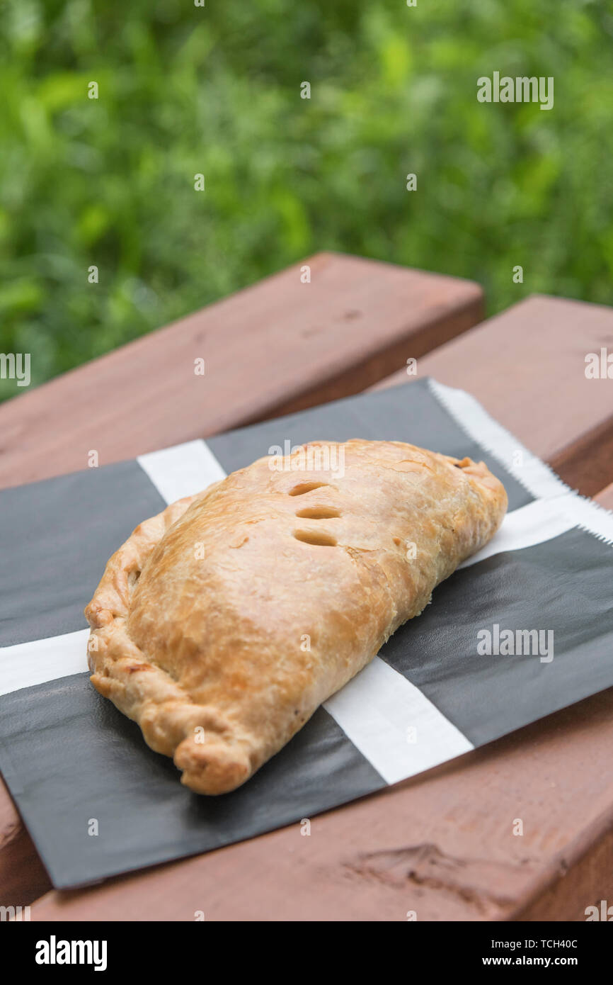 Cornish pasty sitting on paper food bag decorated with St. Piran's flag ...
