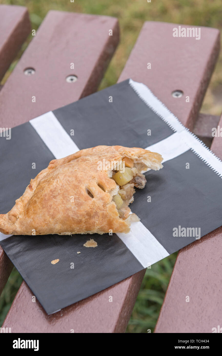 Cornish pasty sitting on paper food bag decorated with St. Piran's flag ...