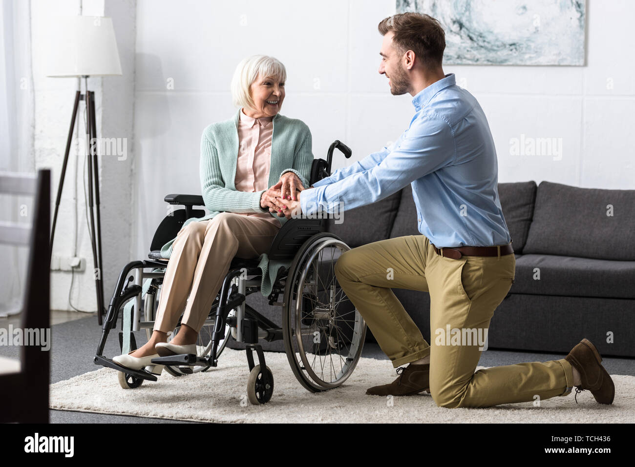 disabled senior woman on wheelchair and smiling man looking at each ...