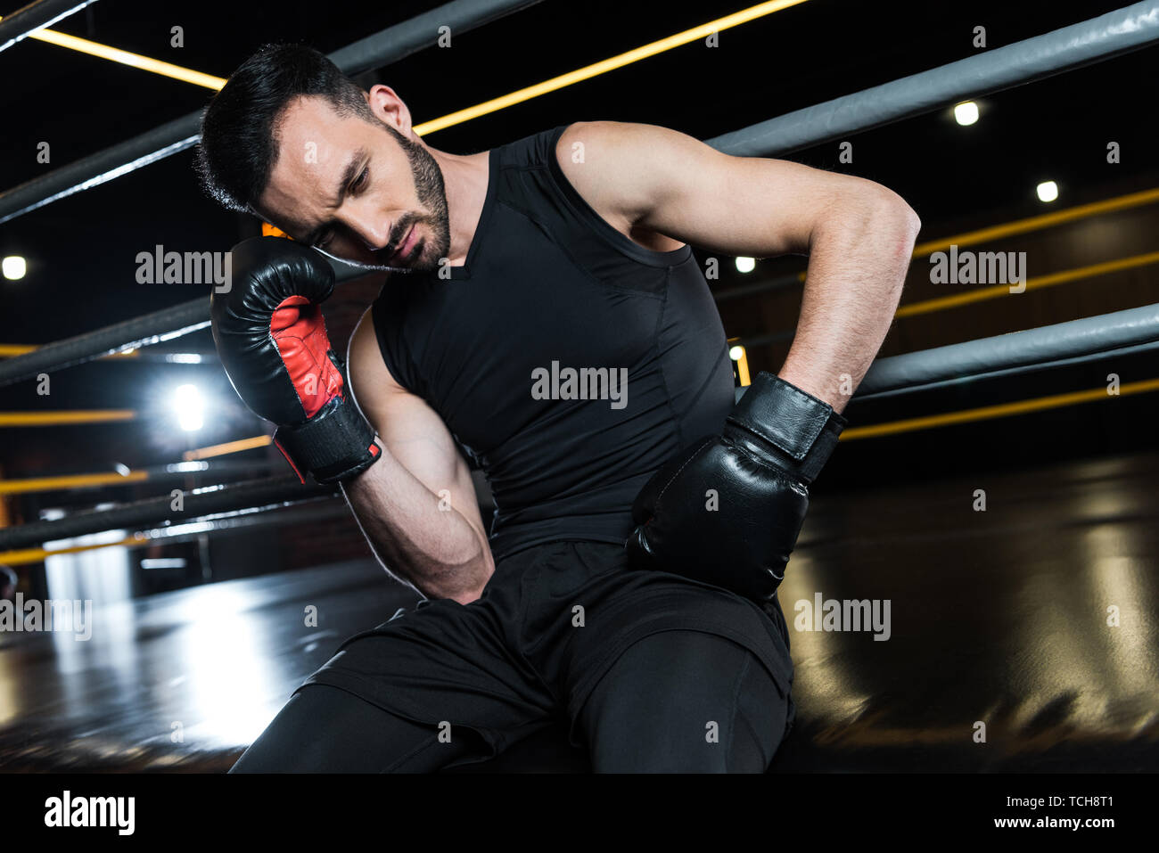 low angle view of tired bearded man in black boxing gloves touching ...