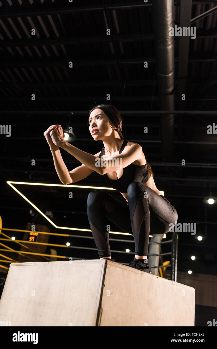 low angle view of attractive woman doing squat exercise on squat box ...