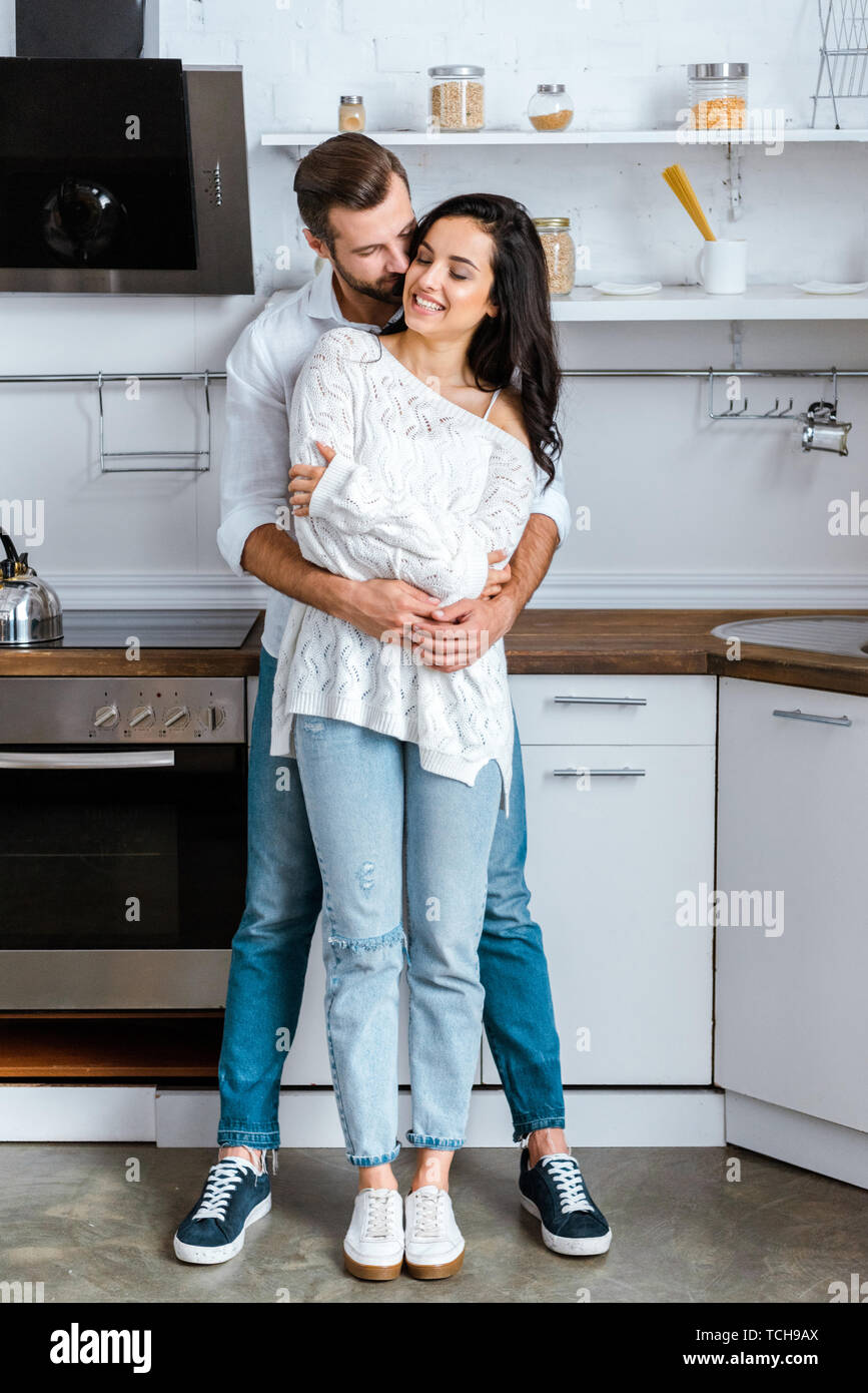 full length view of man gently embracing happy woman at kitchen Stock ...
