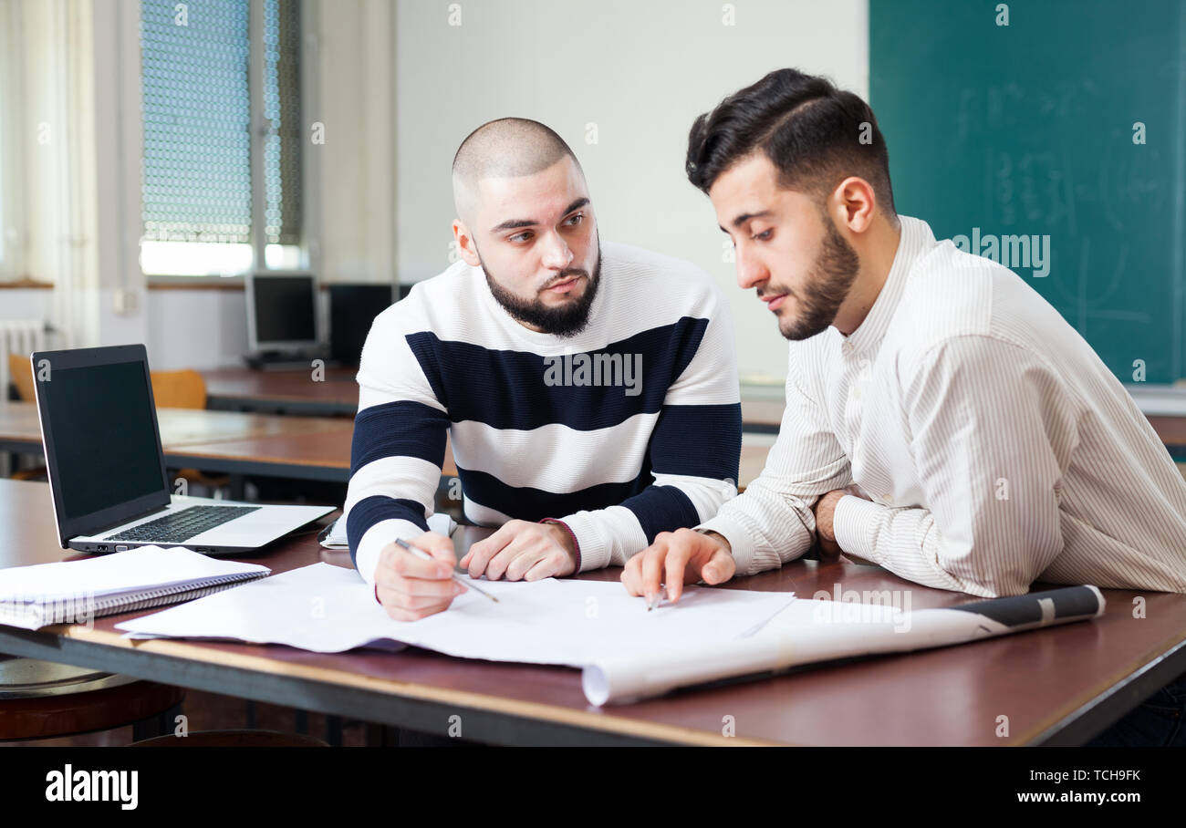 Portrait of two young guys working on their student project at desk in ...