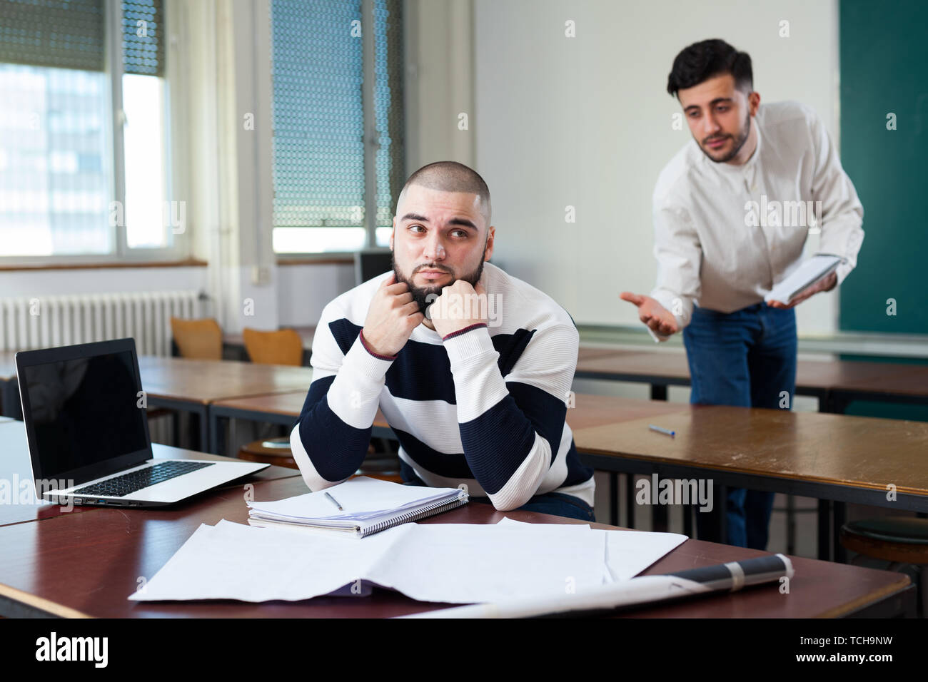 Young man trying to help his worried friend with studies at classroom ...
