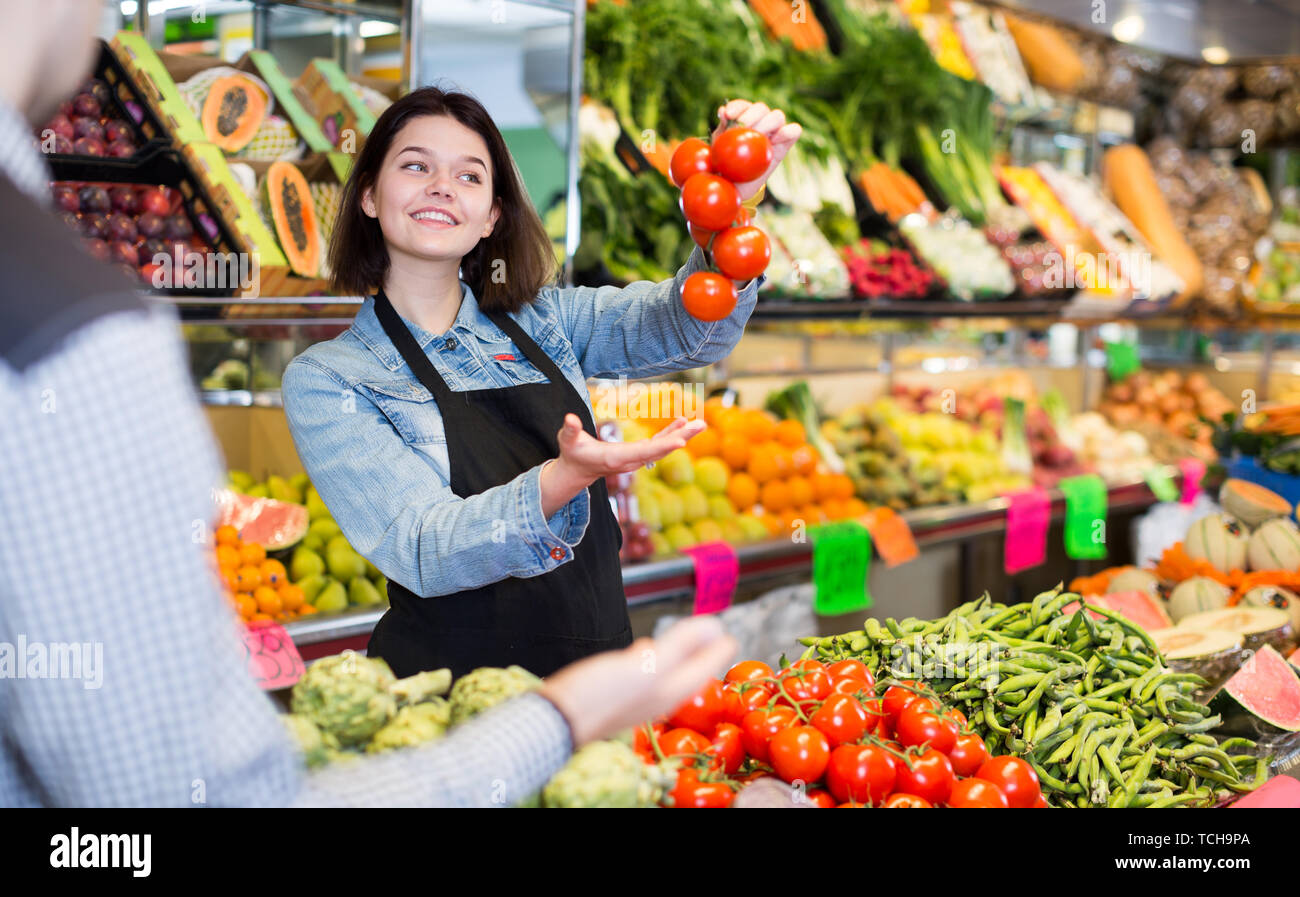Female shopping assistant helping customer to buy tomatoes in grocery ...