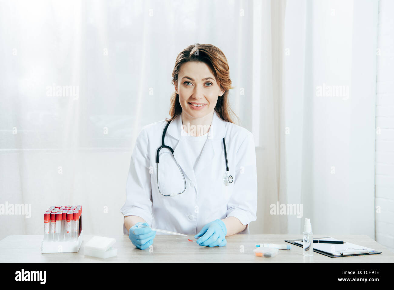 smiling doctor holding pipette and microscope slide with blood sample ...