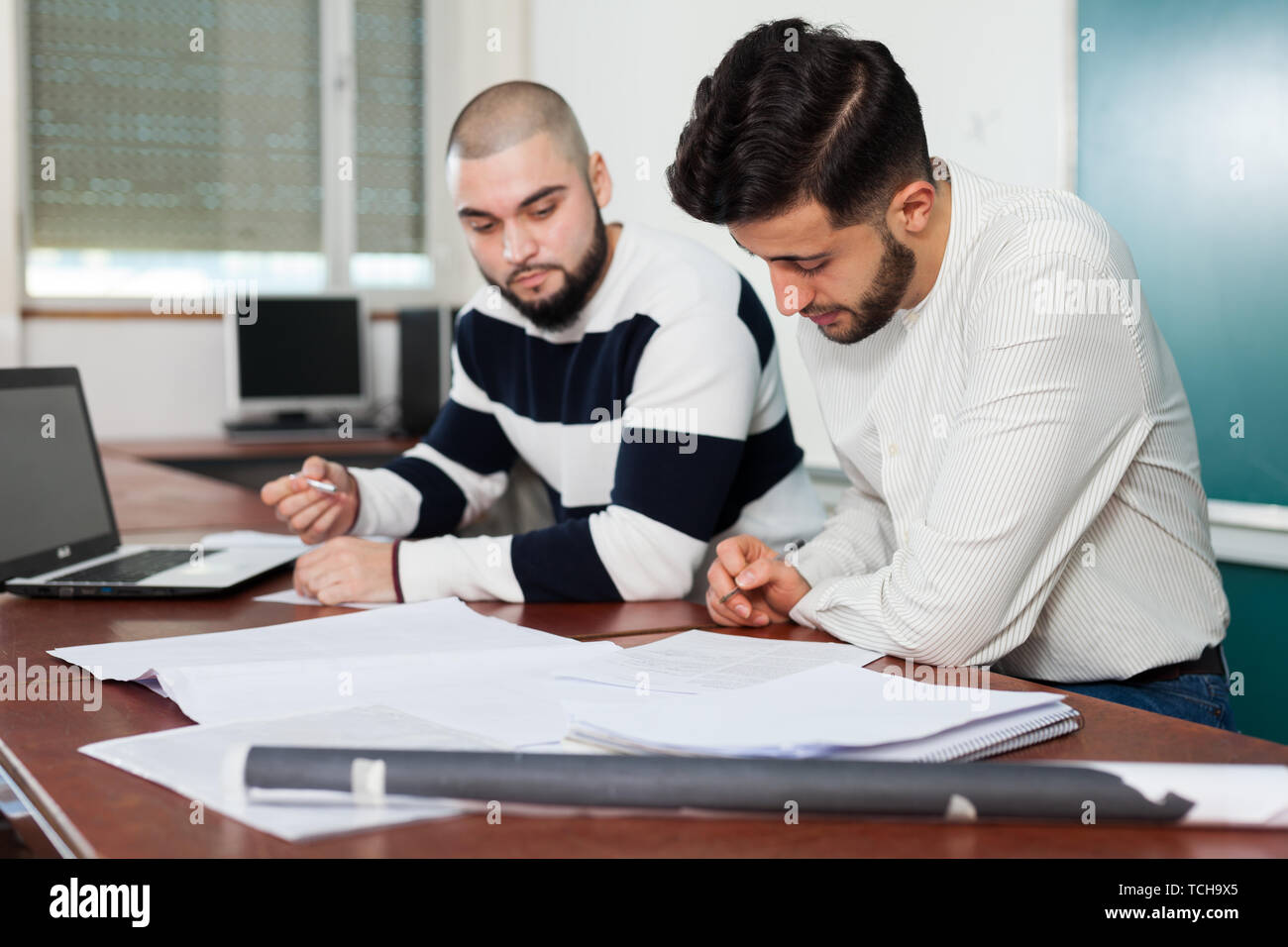 Portrait of two young guys working on their student project at desk in ...