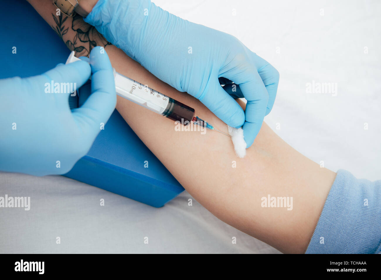 cropped view of donor and doctor with syringe obtaining blood sample ...