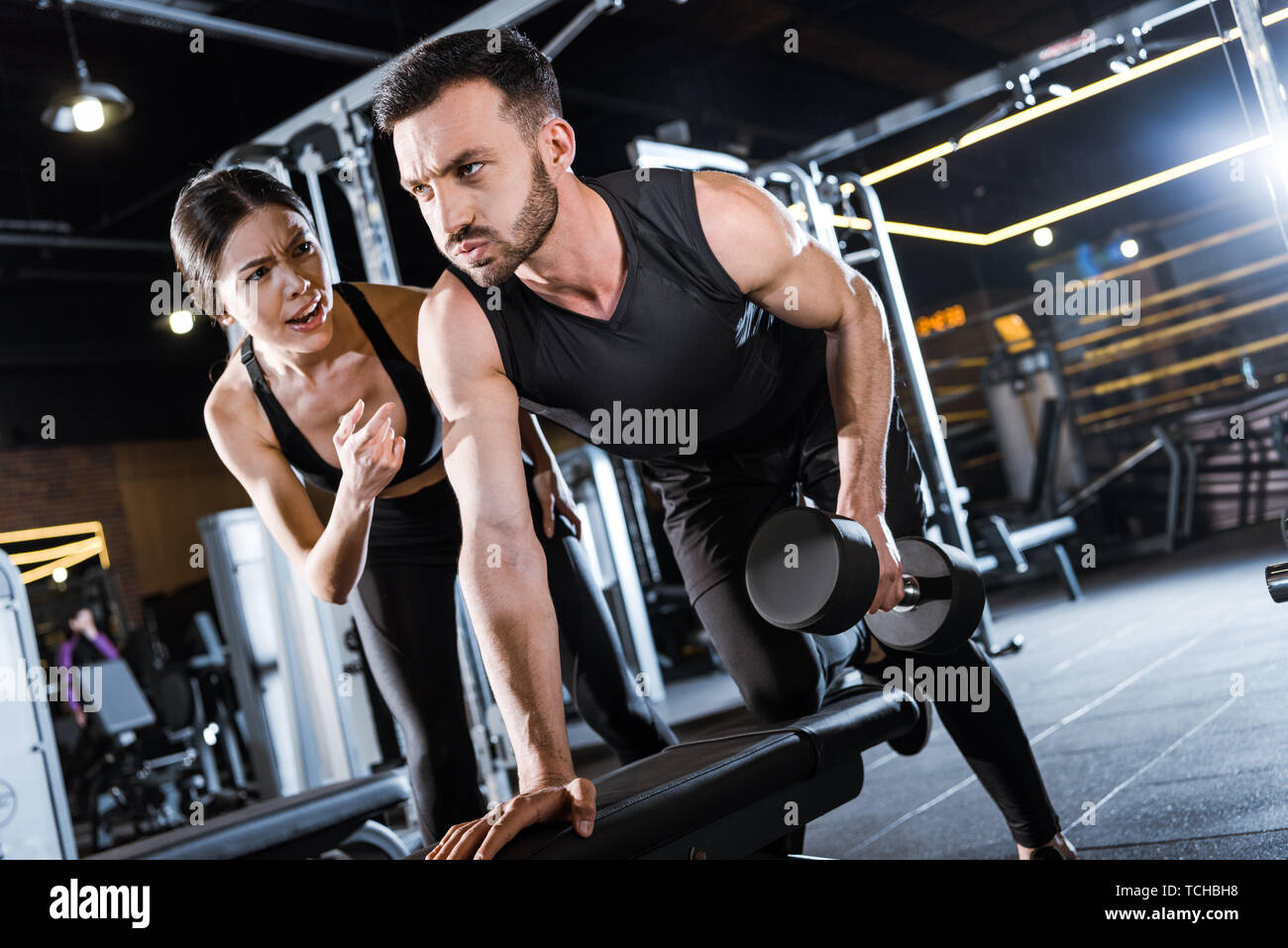 attractive trainer talking with bearded man working out with dumbbell ...