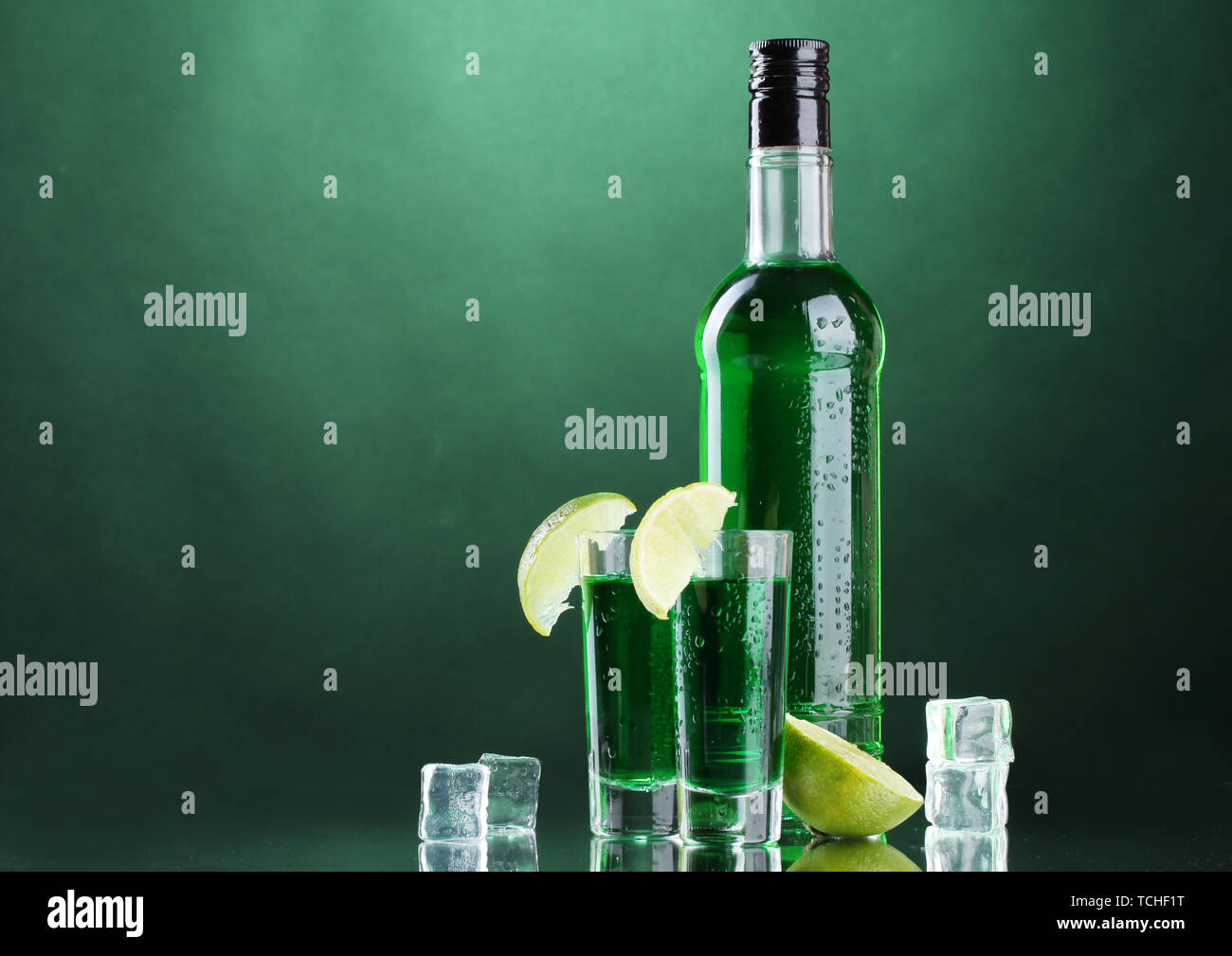 bottle and glasses of absinthe with lime and ice on green background ...