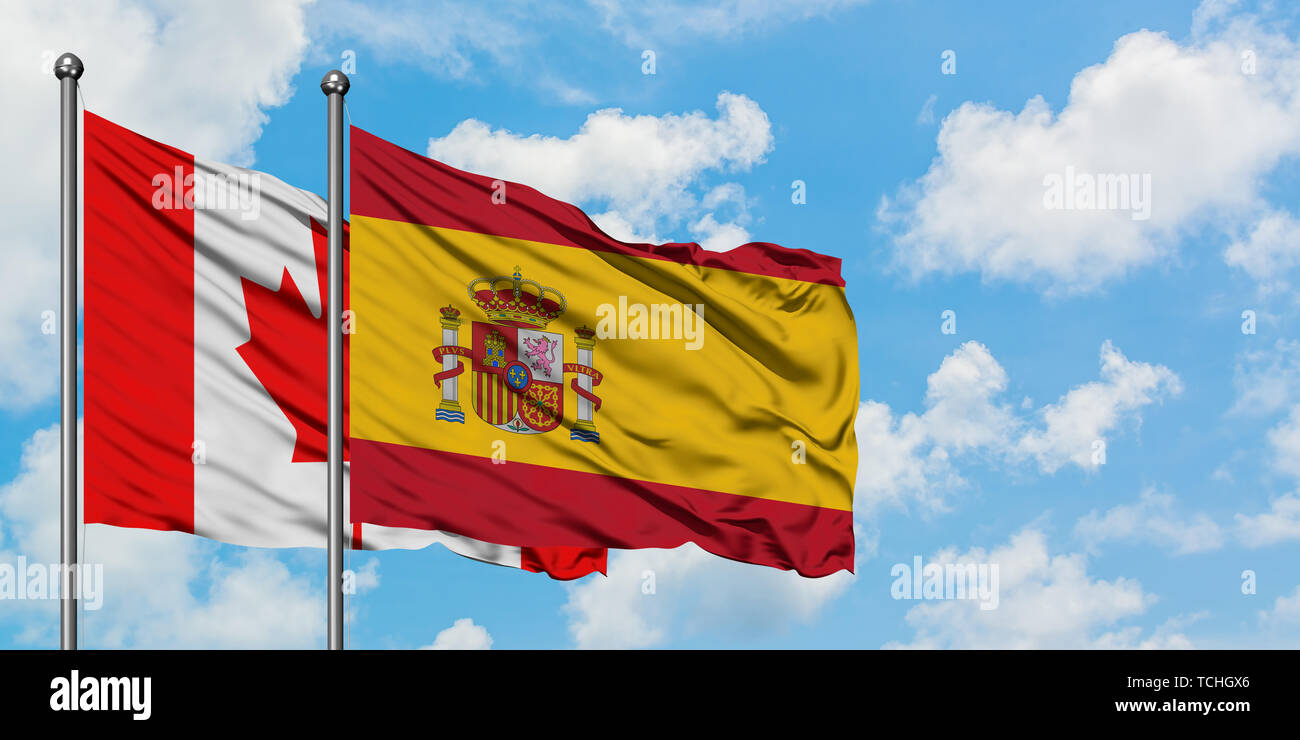 Canada and Spain flag waving in the wind against white cloudy blue sky ...