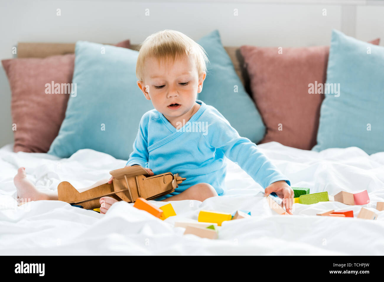 toddler kid playing with wooden biplane near colorful toy blocks on bed ...
